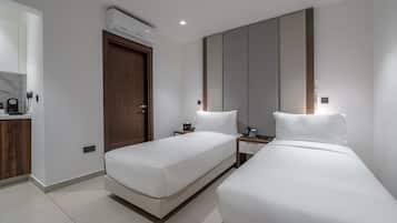 Quarto de hotel com duas camas de solteiro, um guarda-roupa de madeira, um espelho e uma pequena mesa com telefone e chávena.