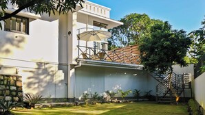 Um edifício moderno com fachada branca, uma varanda com um guarda-sol grande e um gramado bem cuidado.