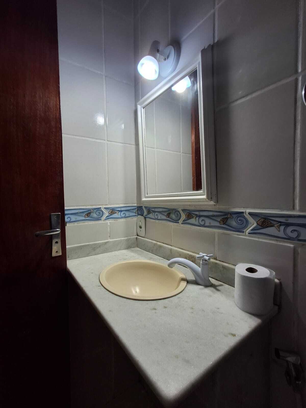 Casa de banho com lavatório branco, espelho e rolo de papel higiénico.