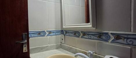 Casa de banho com lavatório branco, espelho e rolo de papel higiénico.