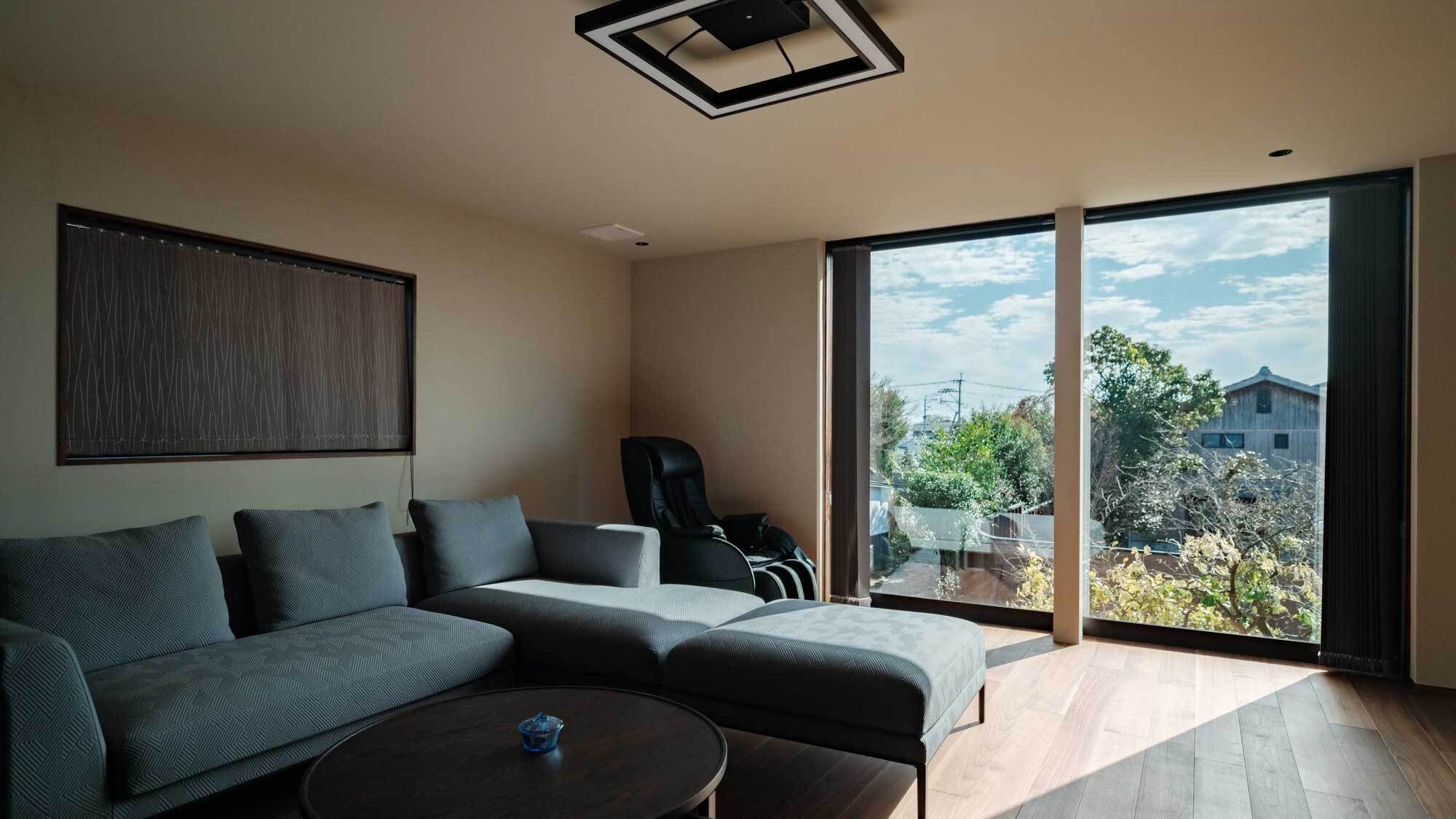 Uma sala de estar moderna com um sofá seccional, uma poltrona de massagem e grandes janelas com vista para o exterior.
