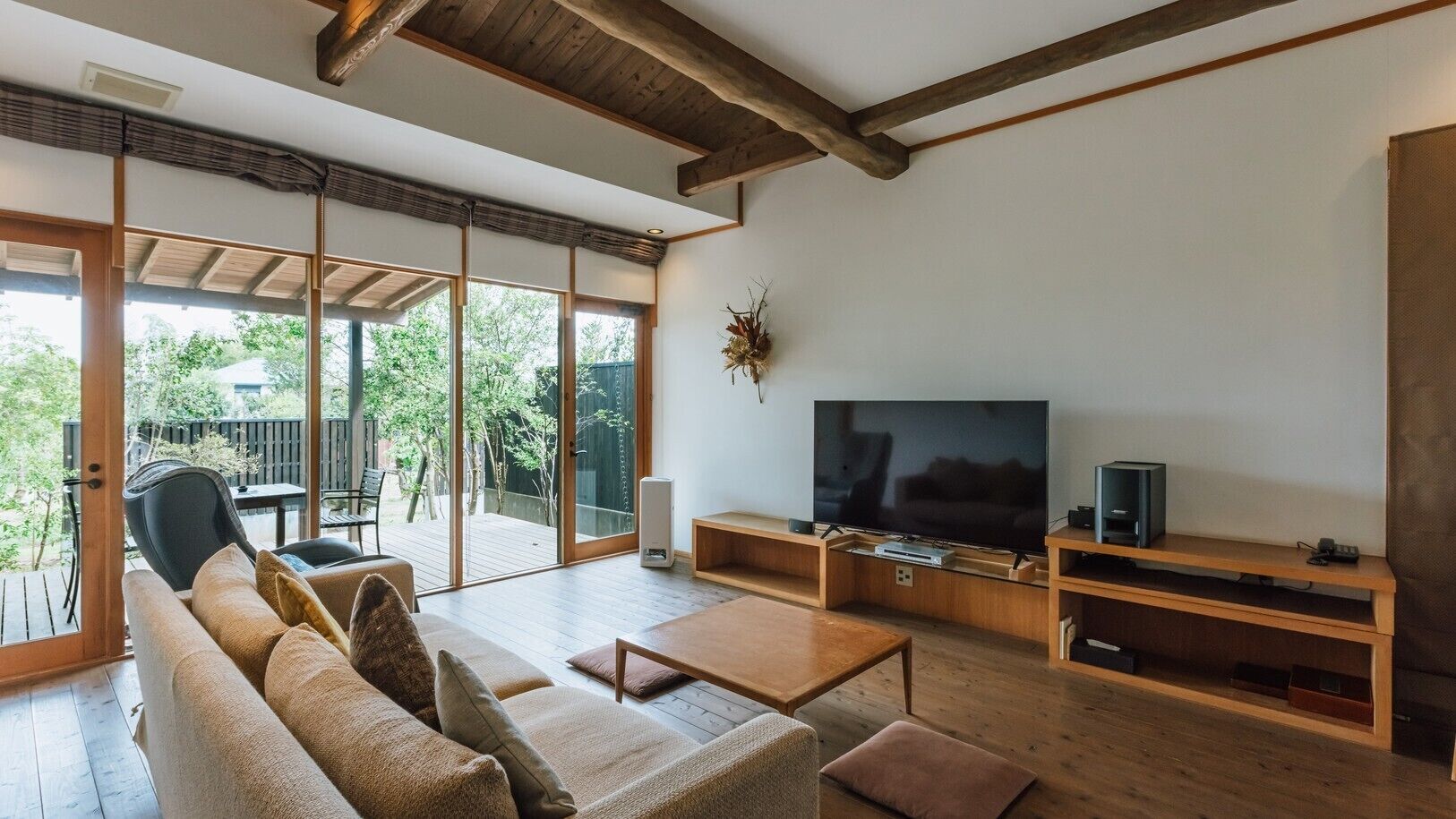 Uma sala de estar moderna com uma televisão grande, mobiliário de madeira e uma porta de vidro deslizante que dá para uma área externa.