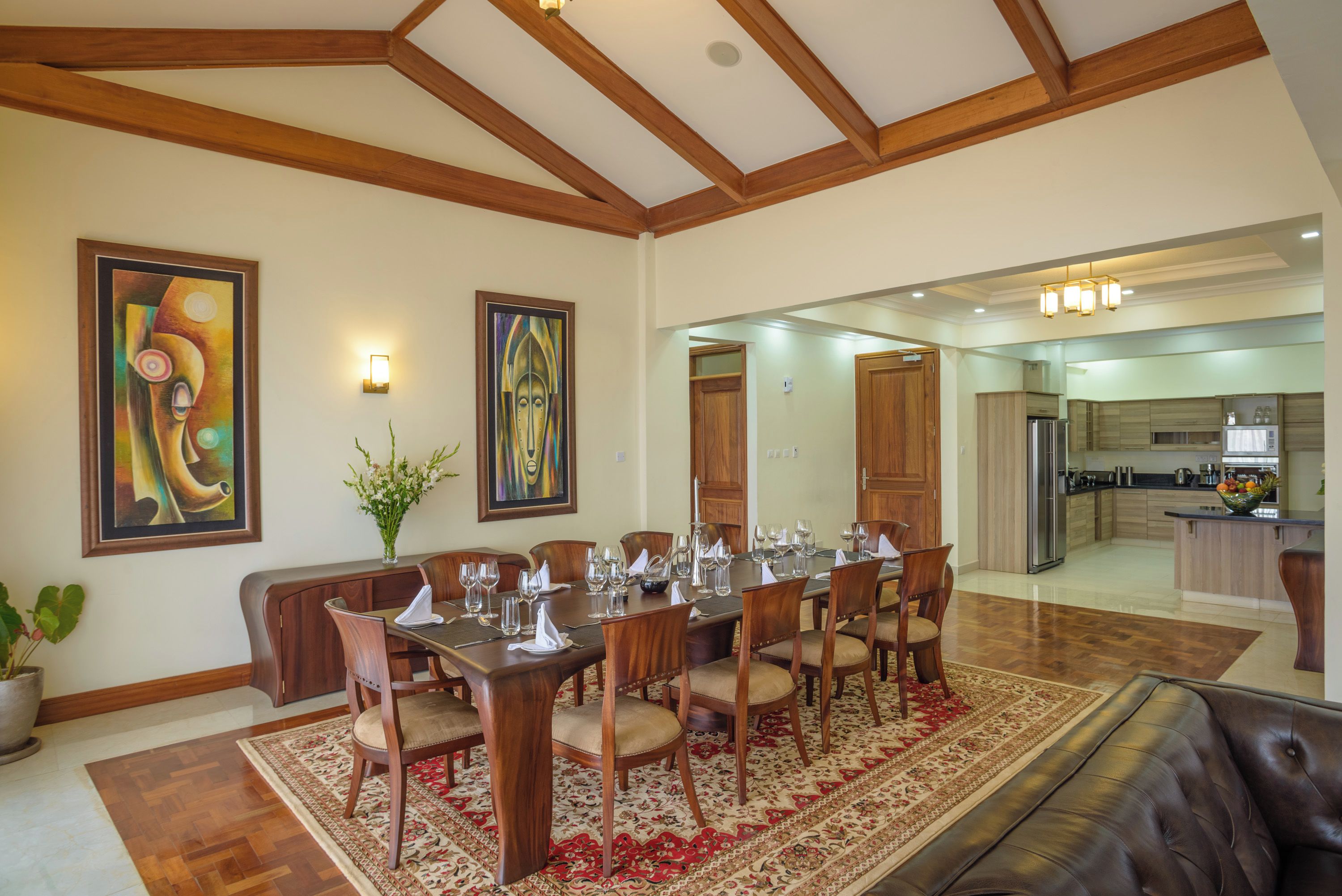 Uma sala de jantar espaçosa com uma longa mesa de madeira posta para uma refeição, ladeada por cadeiras de madeira e um tapete estampado.