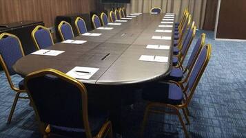 Uma sala de conferência com uma mesa comprida e cadeiras, uma tela de projetor e piso coberto de carpete.