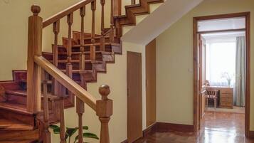 Escadaria de madeira com corrimão, que leva a um quarto com escrivaninha e cadeira.