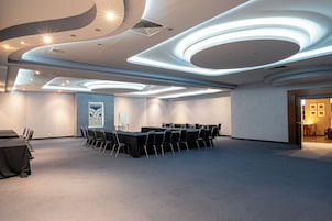 Uma sala de conferências com uma mesa comprida e cadeiras, um quadro branco e um sinal indicando 'Hotel Finis Terre'.