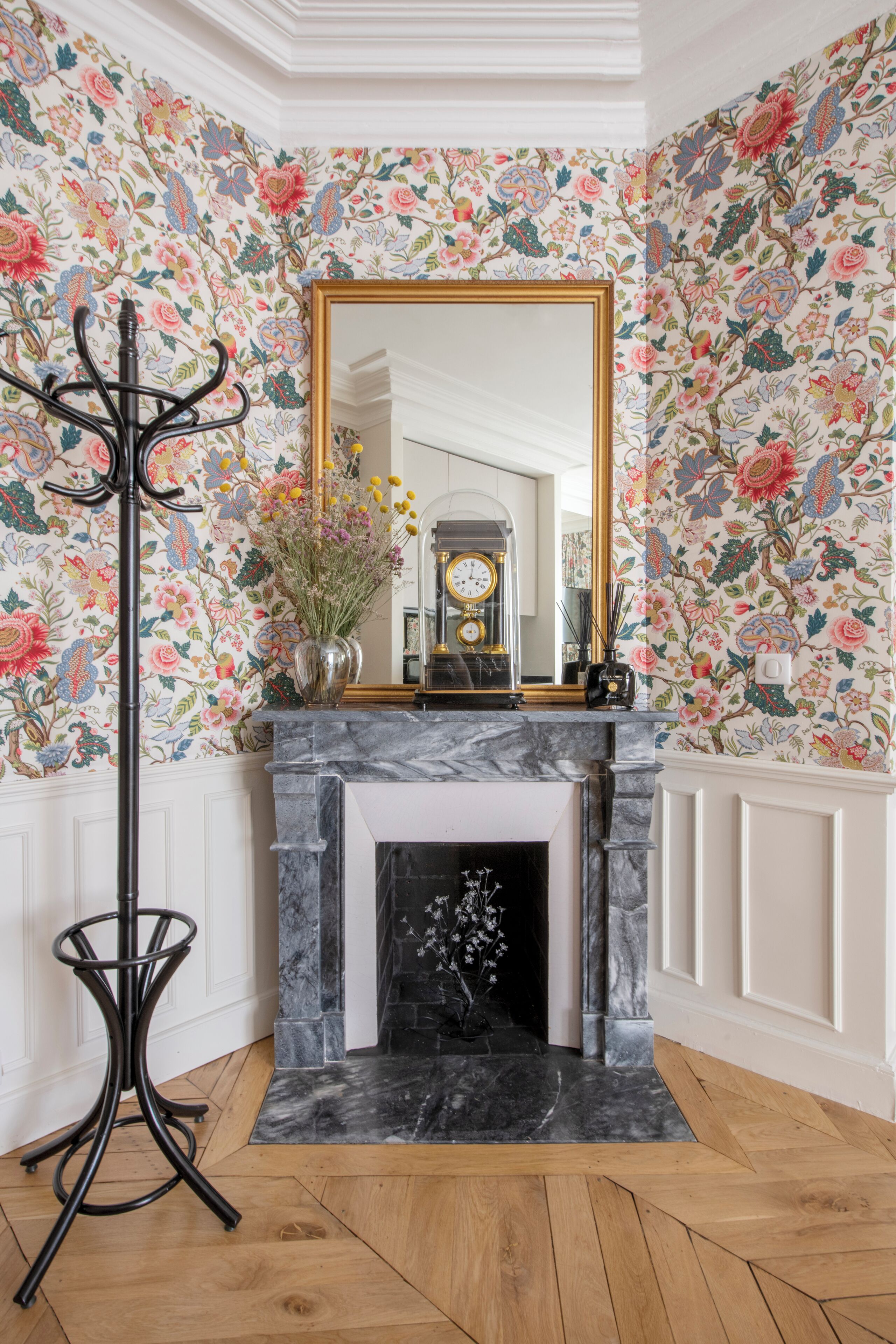 Quarto de canto com lareira, papel de parede floral, um espelho e um relógio.
