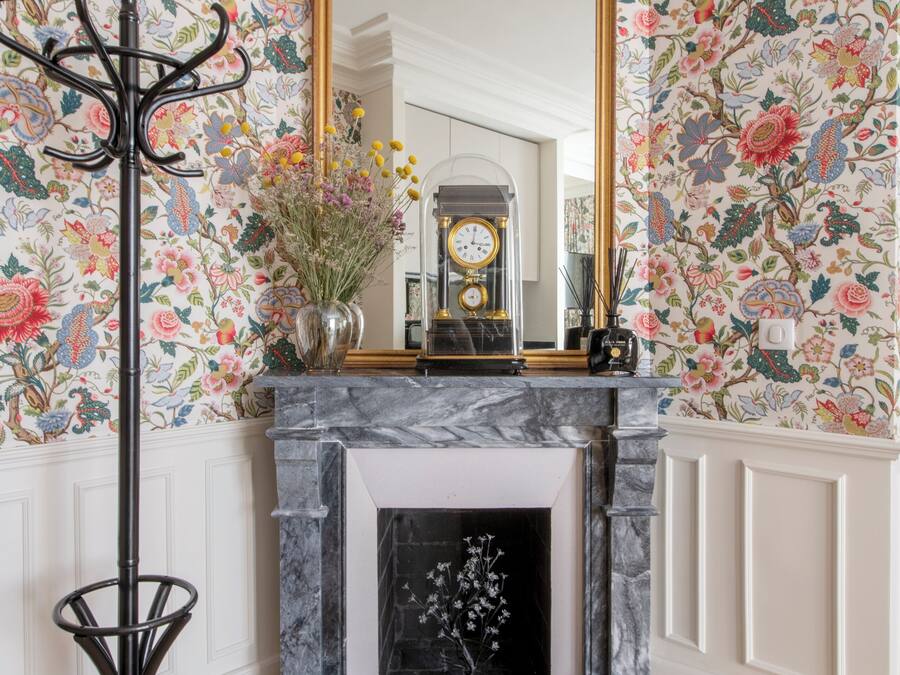 Quarto de canto com lareira, papel de parede floral, um espelho e um relógio.