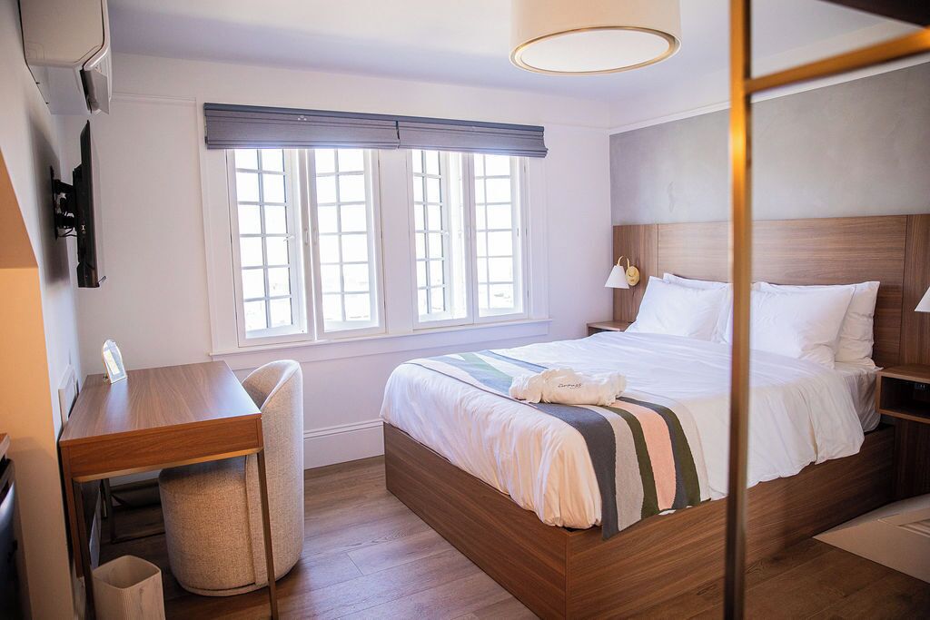 Quarto de hotel com cama de madeira, uma escrivaninha e uma cadeira.