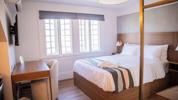 Quarto de hotel com cama de madeira, uma escrivaninha e uma cadeira.
