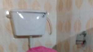 Um banheiro com vaso sanitário, uma toalha rosa no chão e papel de parede estampado.