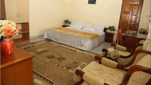 Quarto com cama, mesas de cabeceira, guarda-roupa de madeira, escrivaninha com um vaso e tapete estampado.