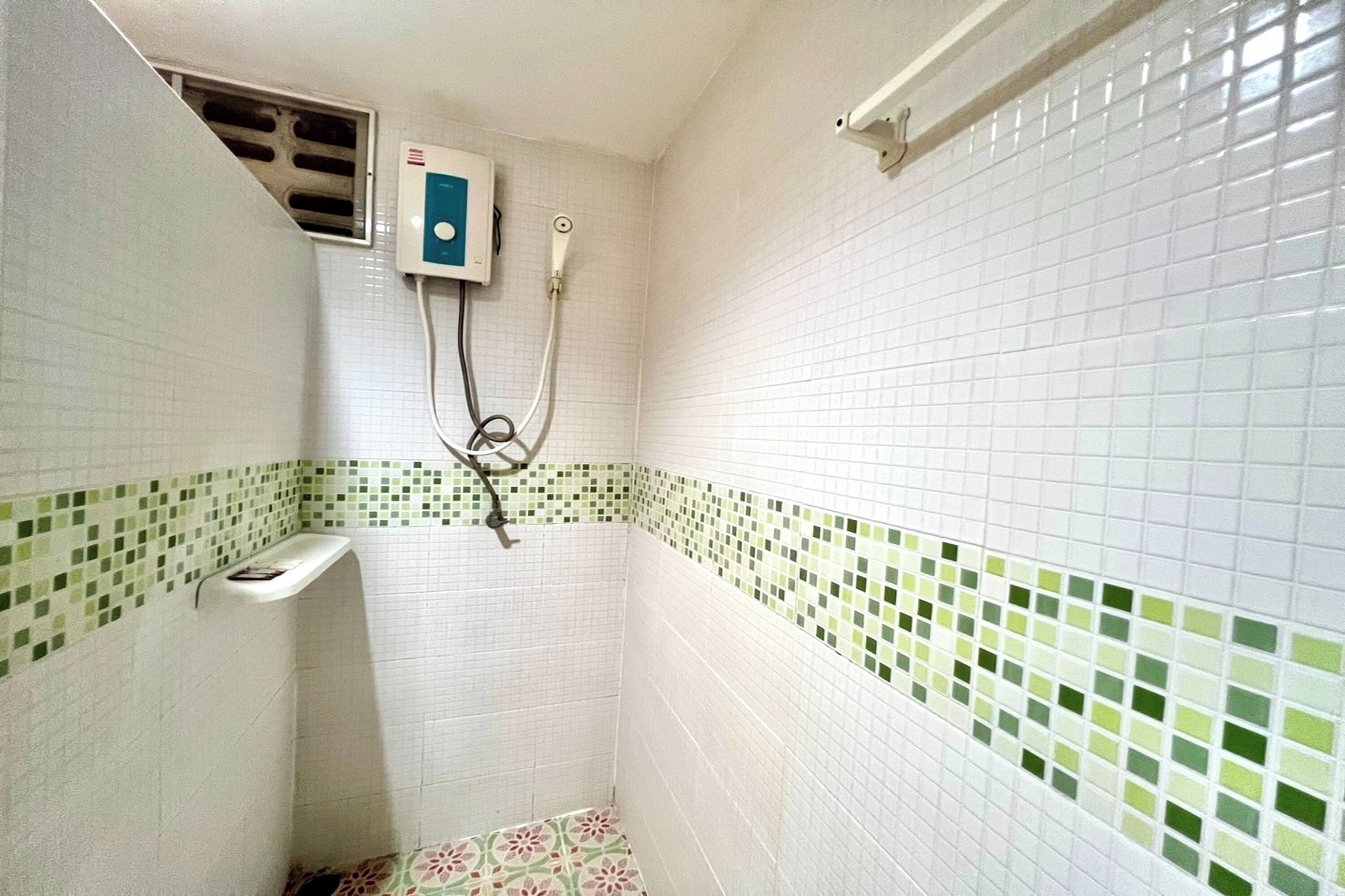 Um banheiro pequeno com azulejos, chuveiro, ar-condicionado fixado na parede e uma prateleira com um livro.