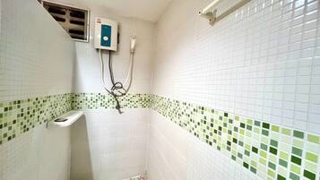 Um banheiro pequeno com azulejos, chuveiro, ar-condicionado fixado na parede e uma prateleira com um livro.