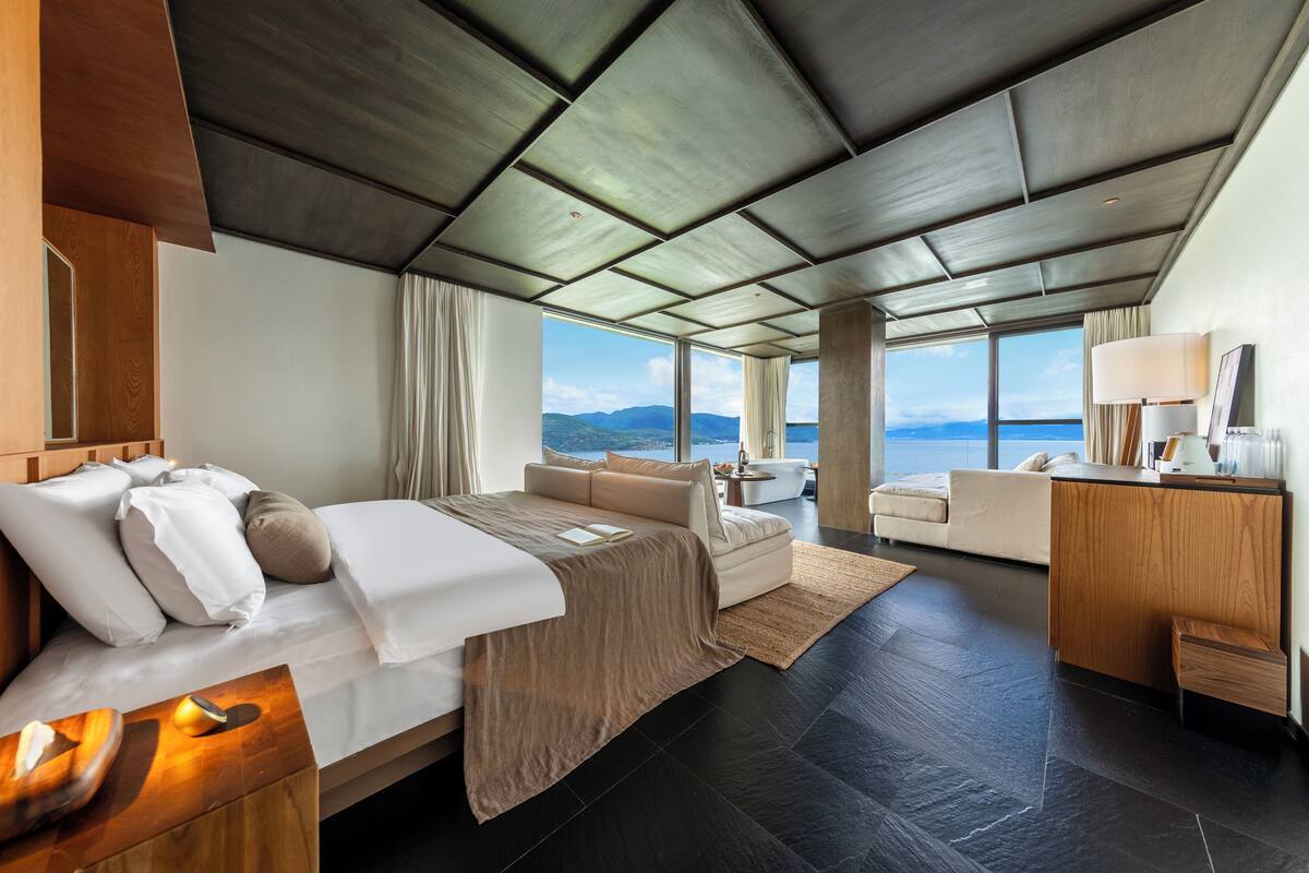 Quarto de hotel moderno com uma cama grande, um sofá, uma escrivaninha e vista para as montanhas.