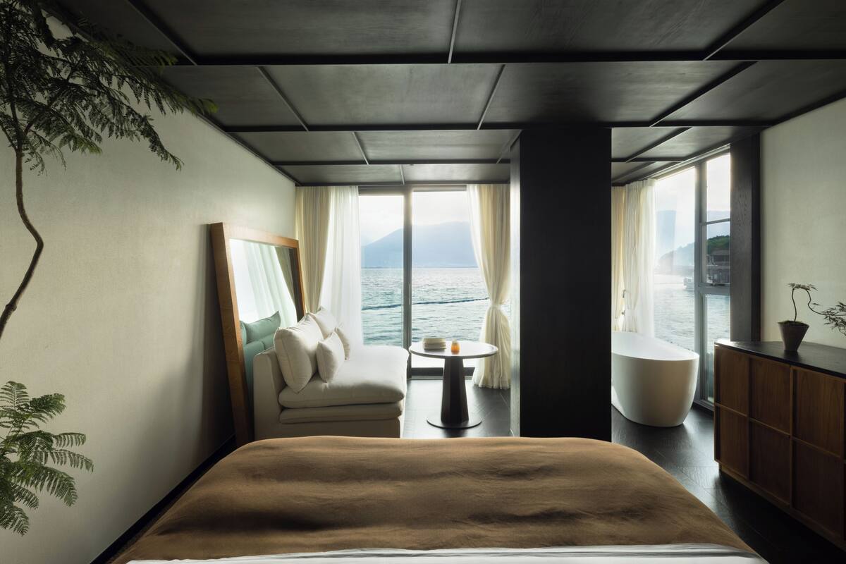 Quarto de hotel moderno com uma cama grande, um sofá, uma mesa redonda, uma banheira e vista para o mar.