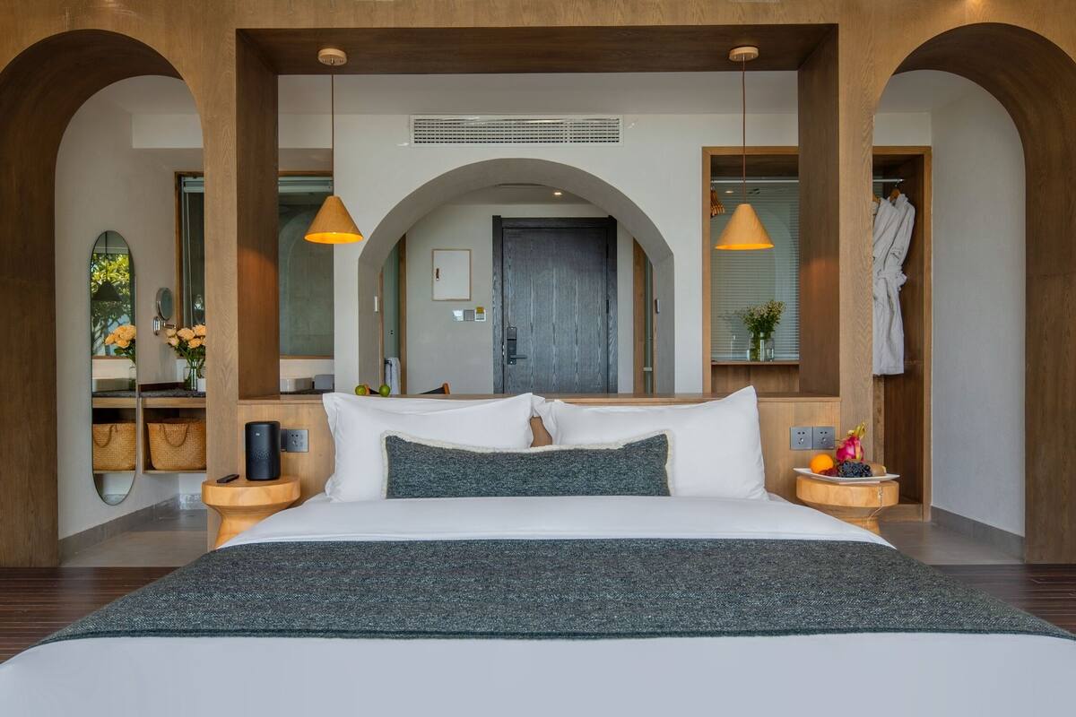 Quarto de hotel moderno com uma cama grande, arcos de madeira e um espelho refletindo o ambiente.
