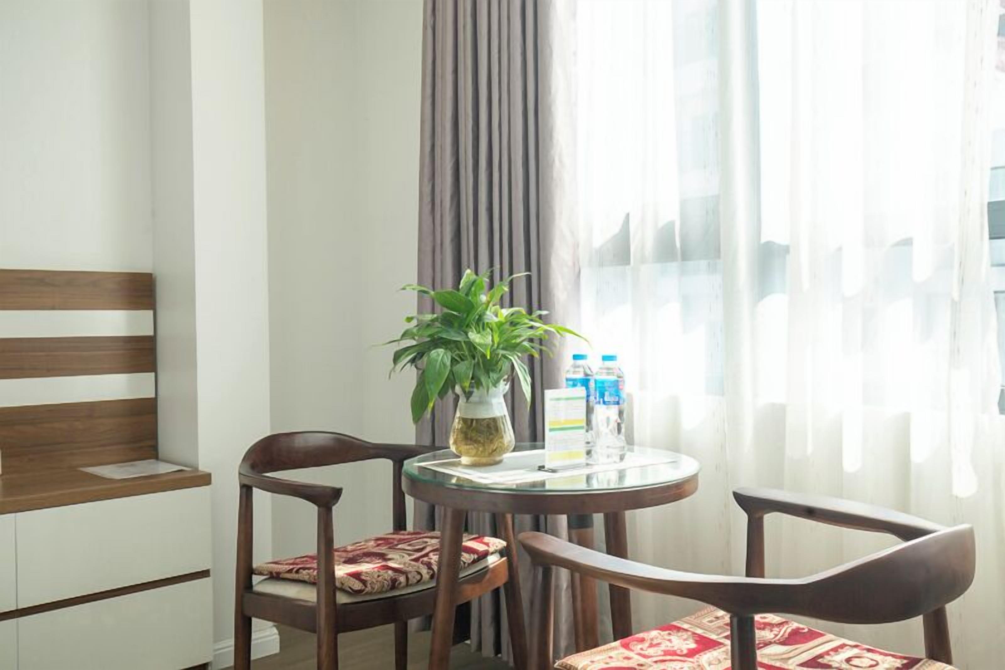 Quarto com uma mesa de vidro redonda, duas cadeiras de madeira, uma planta em vaso e uma garrafa de água.