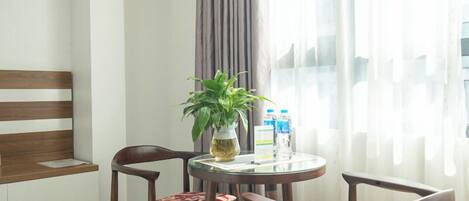Quarto com uma mesa de vidro redonda, duas cadeiras de madeira, uma planta em vaso e uma garrafa de água.