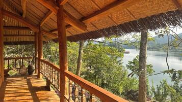 Um deck de madeira com telhado de palha com vista para um lago.