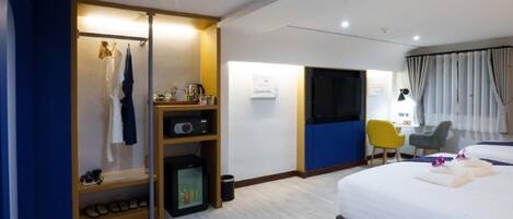 Quarto de hotel com uma cama, escrivaninha, cadeira, guarda-roupa e televisão.