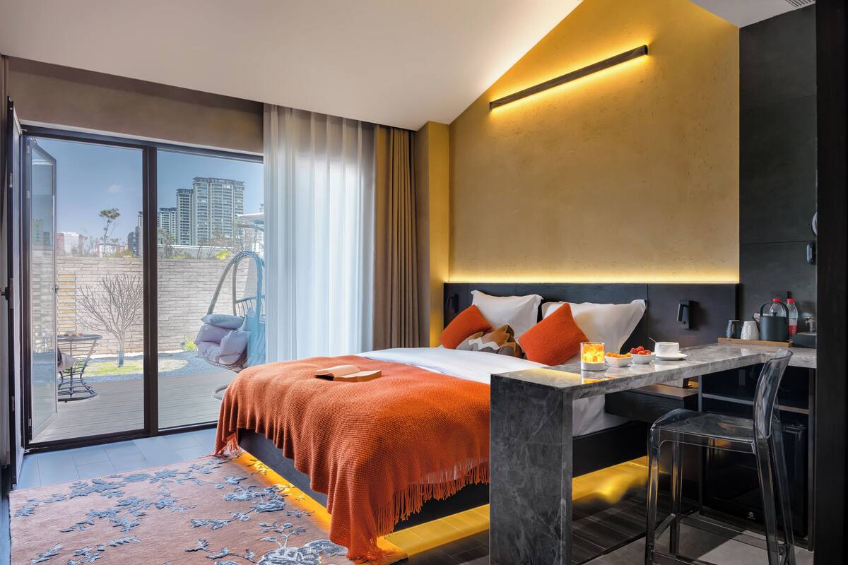 Quarto de hotel moderno com uma cama grande, uma escrivaninha e vista da cidade através da porta de vidro.
