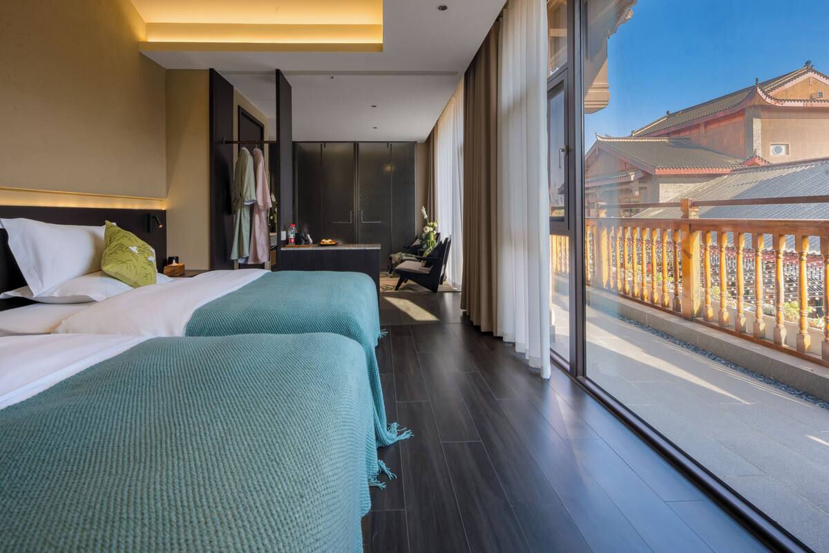 Quarto de hotel moderno com duas camas, uma varanda e vista para arquitetura chinesa tradicional, além de uma janela grande.