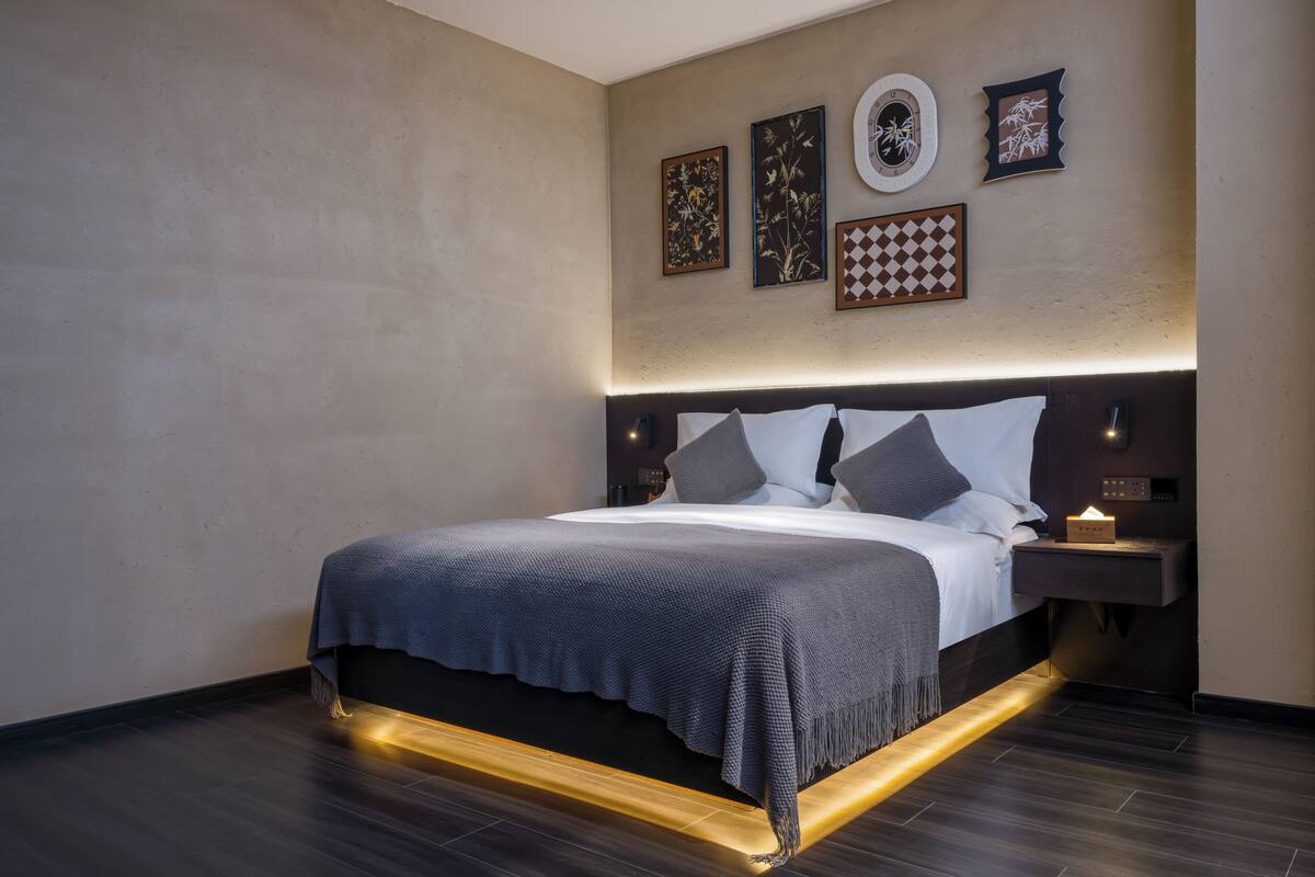 Um quarto moderno com uma cama grande, uma mesa de cabeceira com abajur e uma obra de arte pendurada na parede.