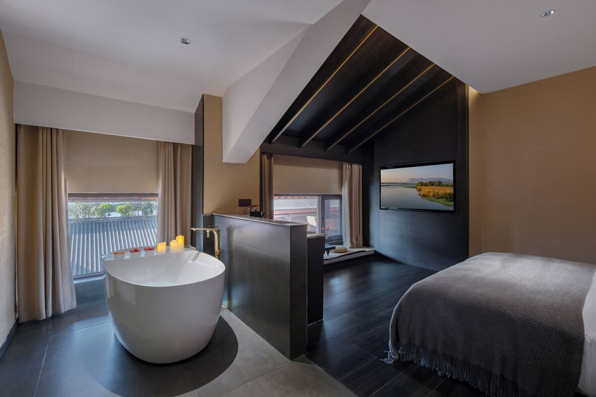 Quarto de hotel moderno com uma banheira grande, uma cama, TV fixada na parede e varanda com vista.