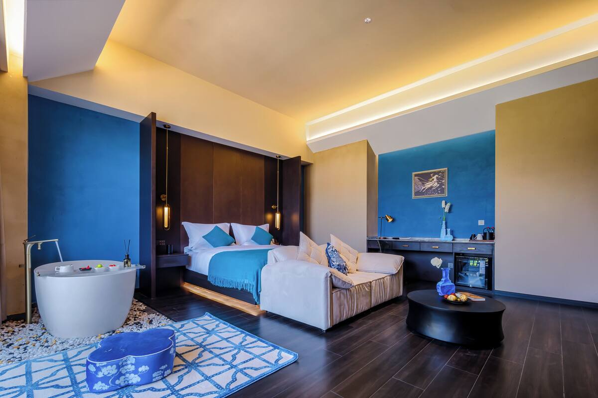 Quarto de hotel moderno com uma cama grande, área de estar, cozinha compacta e banheira.