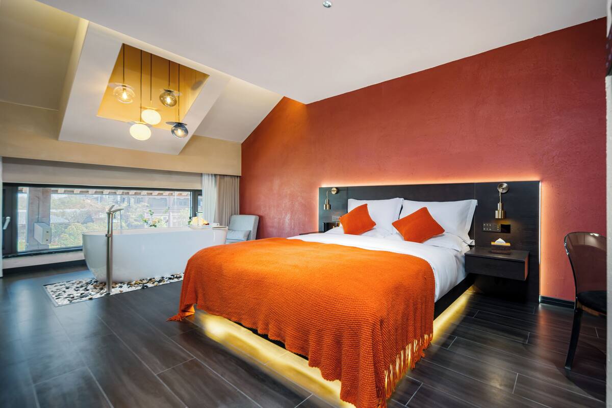 Quarto de hotel moderno com uma cama grande, uma banheira e vista para a cidade.