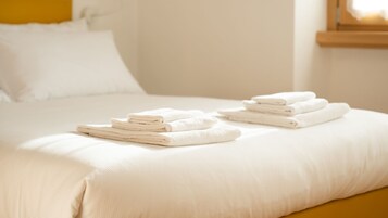 Cama bem arrumada com toalhas brancas dobradas e um travesseiro branco.