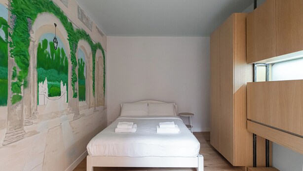 Quarto com uma cama, mesa de cabeceira e guarda-roupa.