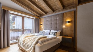Quarto com cama grande, vigas de madeira no teto, vista para o exterior e duas luzes fixadas na parede.