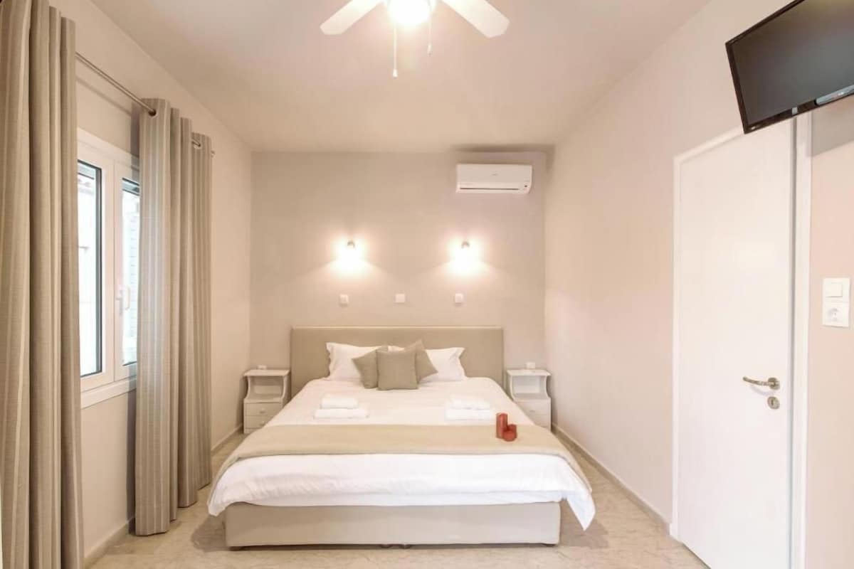Quarto de hotel com cama, mesas de cabeceira, ventilador de teto, ar condicionado e televisão fixada na parede.