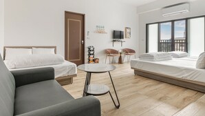 Quarto de hotel moderno com duas camas, um sofá, uma mesinha redonda, televisão e varanda com vista.