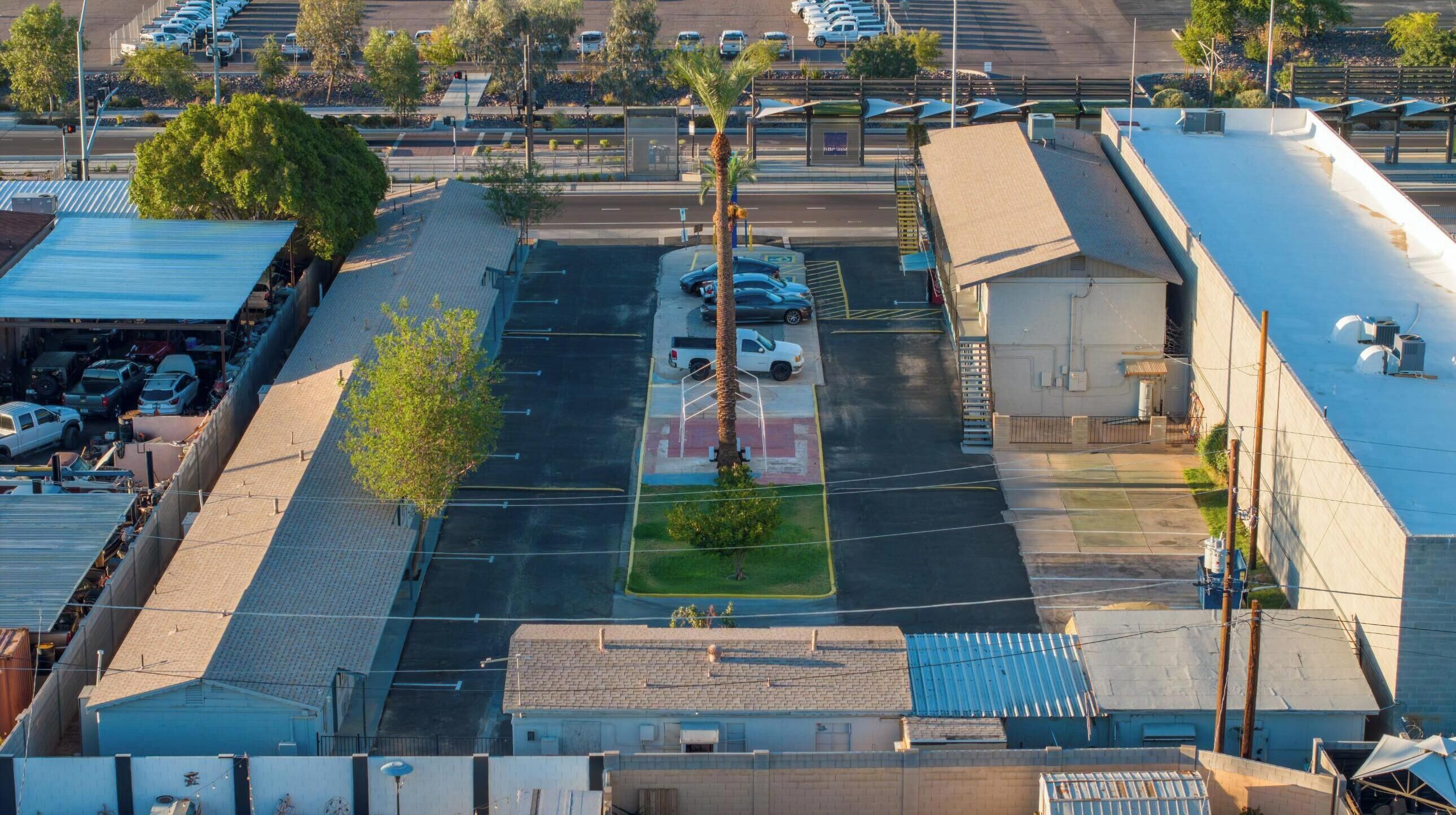 Vista aérea de um estacionamento com vários carros, uma palmeira e um edifício com telhado azul.