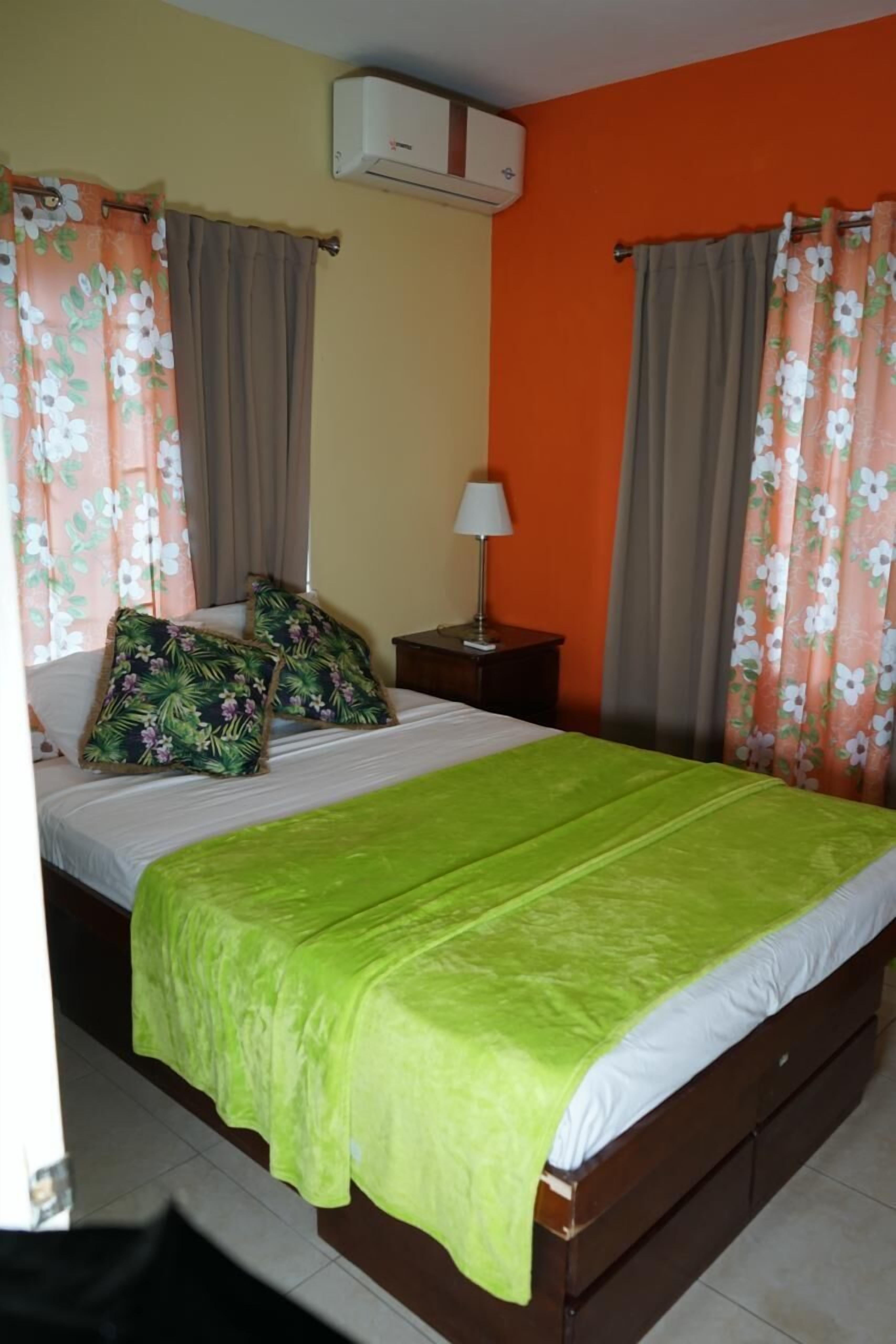 Quarto com cama, duas almofadas, mesa de cabeceira com abajur e ar condicionado.