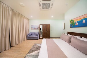 Quarto com uma cama grande, um sofá, um quadro e uma porta que dá para outro espaço.