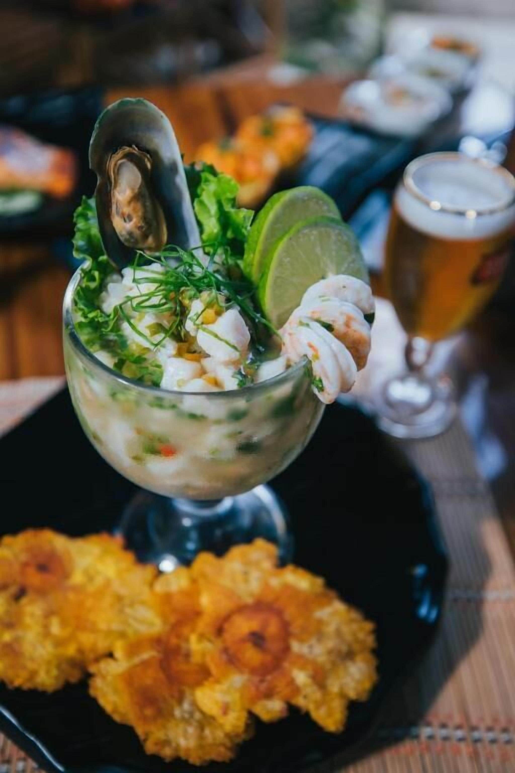 Prato de frutos do mar com concha de amêijoa, limão e ervas, acompanhado de banana frita e um copo de cerveja.