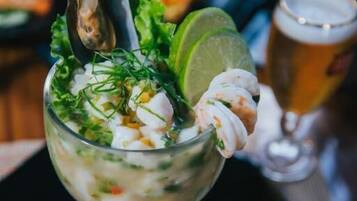 Prato de frutos do mar com concha de amêijoa, limão e ervas, acompanhado de banana frita e um copo de cerveja.