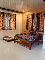 Quarto com cama de madeira, uma pequena mesa de cabeceira e cortinas com padrão de folhas.