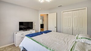 Quarto com cama, televisão sobre uma cômoda e armário com portas brancas.