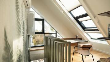 Quarto estilo loft moderno, com janelas no teto, escrivaninha de madeira e uma cadeira.