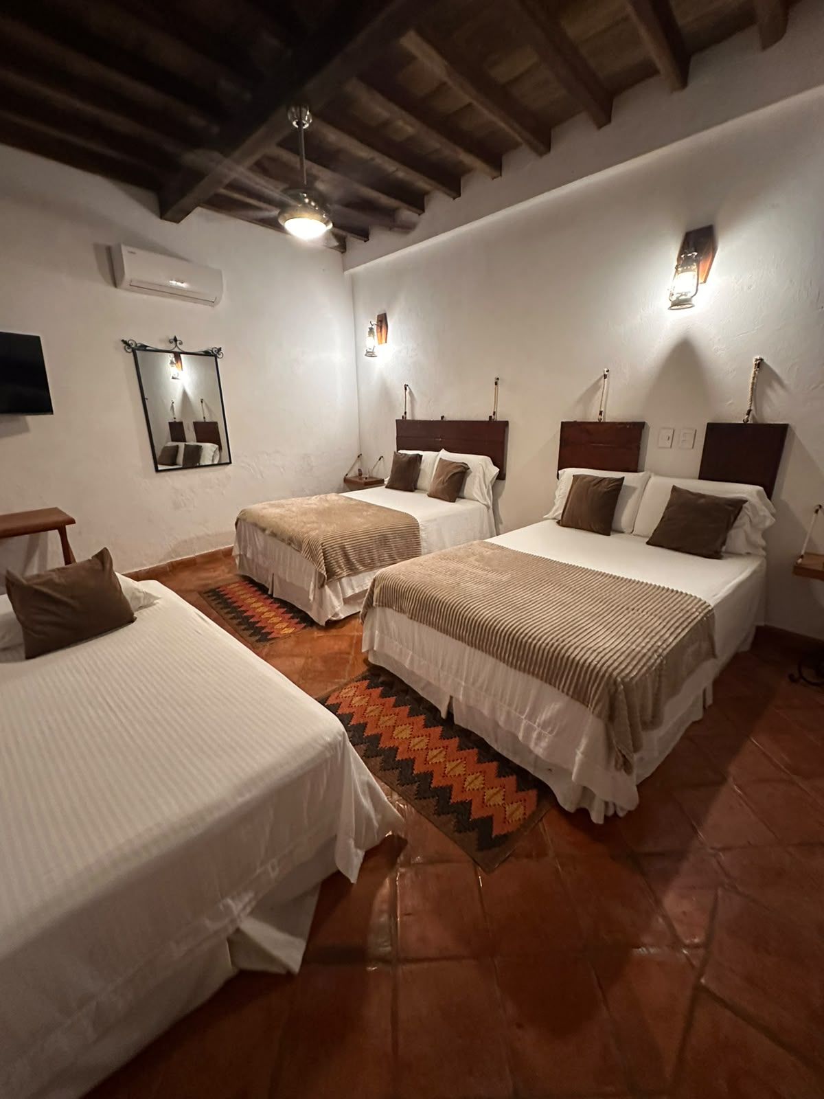 Quarto de hotel com duas camas, um espelho, televisão de tela plana e ventilador de teto.
