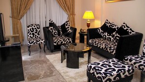 Uma sala de estar com sofá, poltronas, mesa de centro e televisão.