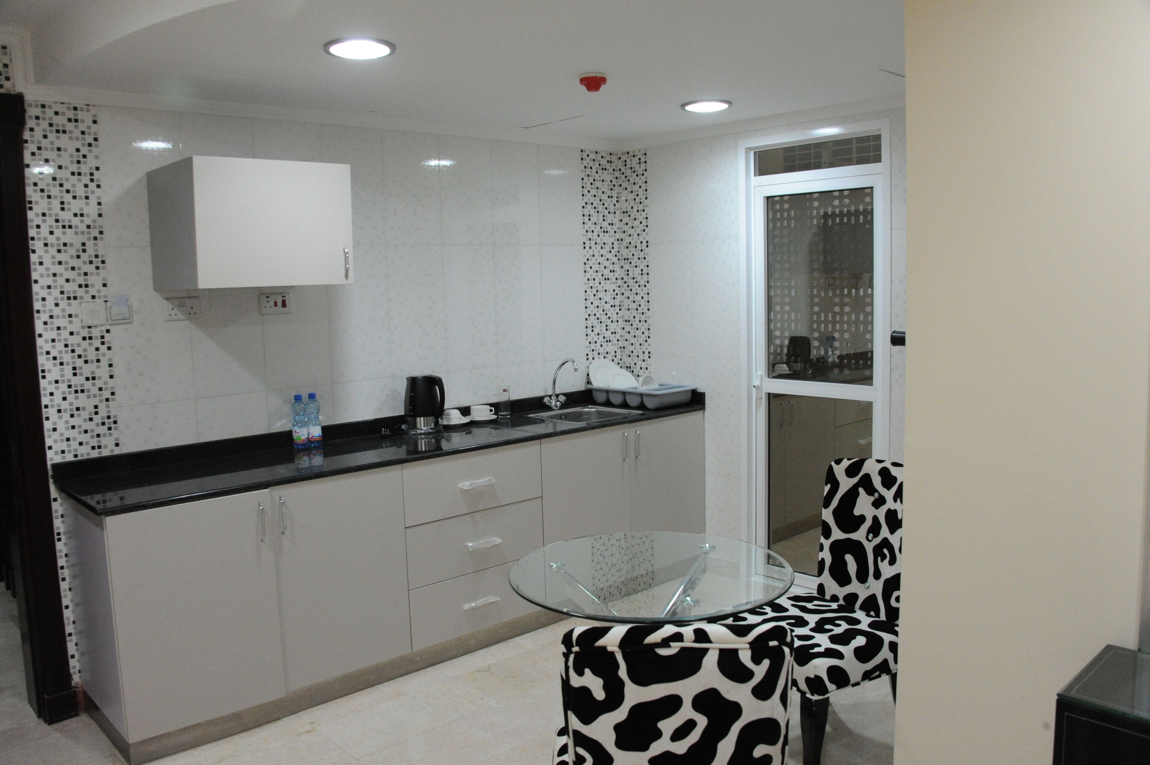 Cozinha moderna com armários brancos, bancada preta e uma mesa de vidro com cadeira de estampa de leopardo.