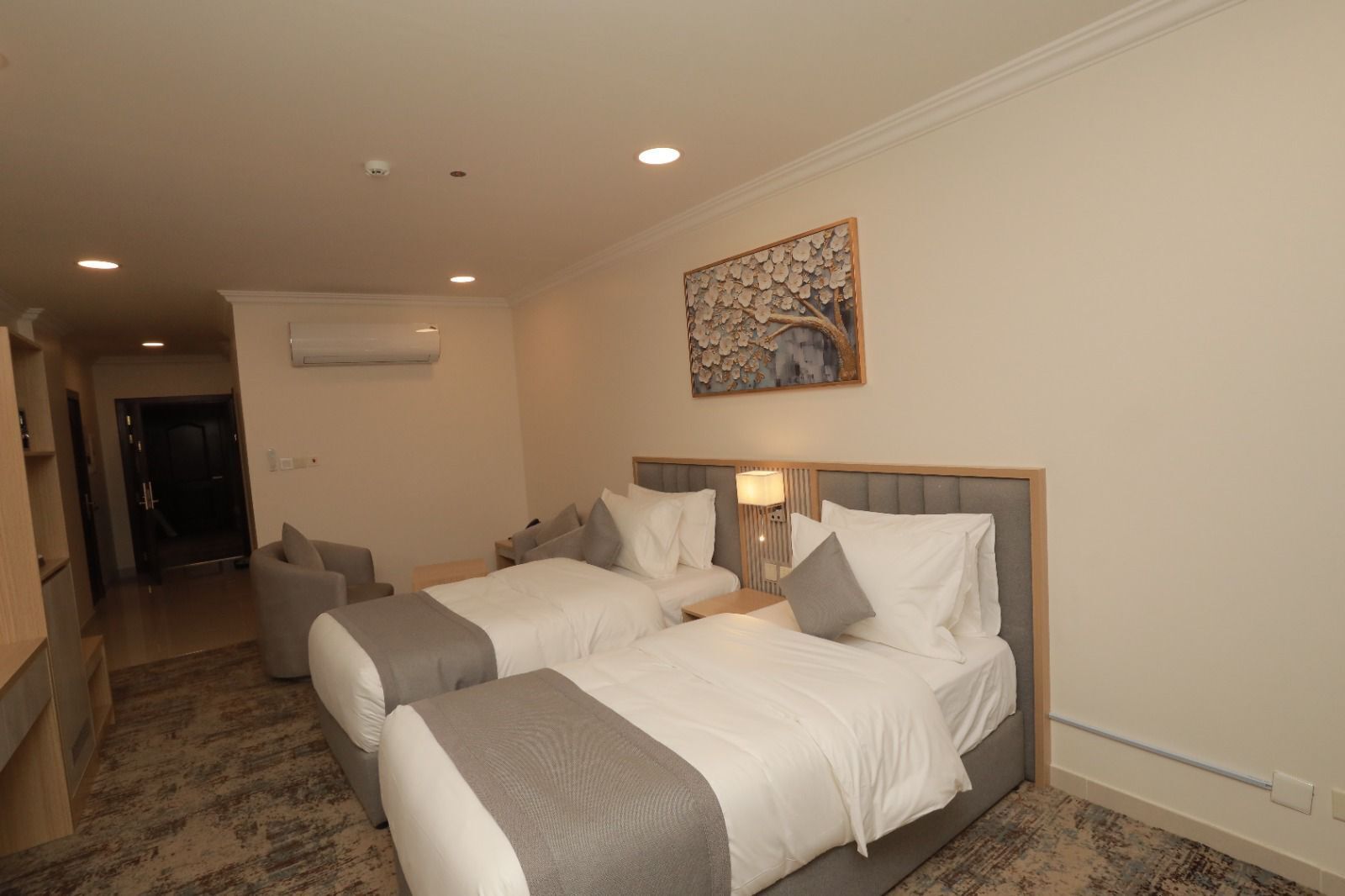 Quarto de hotel com duas camas, um sofá, um quadro e um ar condicionado.
