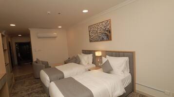 Quarto de hotel com duas camas, um sofá, um quadro e um ar condicionado.
