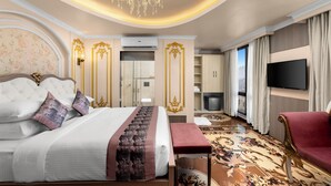 Quarto de hotel luxuoso com uma cama grande, uma poltrona vermelha, televisão e vista para a cidade.